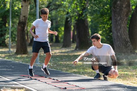 소년은 민첩성 사다리를 사용하여 트레이너와 함께 야외에서 운동합니다 이 세션은 전문가의 지도하에 재미있고 매력적인 환경에서 조정력 속도 및 체력을 촉진합니다 18 19세에