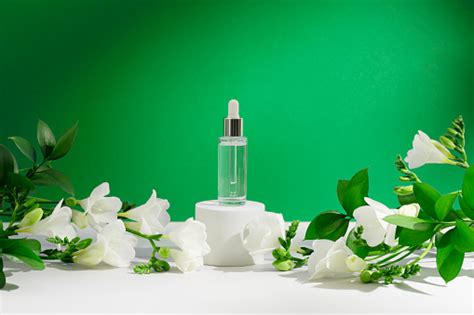 흰색 연단에 스포이드 병에 담긴 페이셜 세럼은 녹색 배경에 프리지어 꽃 나뭇잎 그림자가 있습니다 천연 스킨 케어 화장품 모형 브랜딩 또는 프레젠테이션을 위한 받침대의 미용