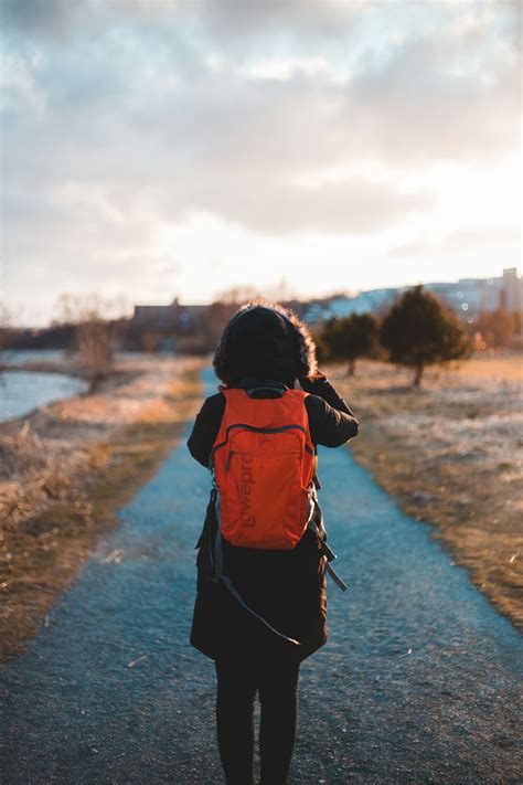주황색과 검은색 후드티를 입은 남자가 낮에 비포장 도로에 서 있다 사진 Unsplash의 무료 갈색 이미지