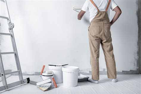 한 남자가 롤러로 하얀 벽을 그립니다 내부의 수리 빈 방에 벽을 그리는 젊은 남성 데코레이터 개념 빌더 또는 빈 방에 페인트 롤러와 헬멧에 화가 40 44세에 대한 스톡