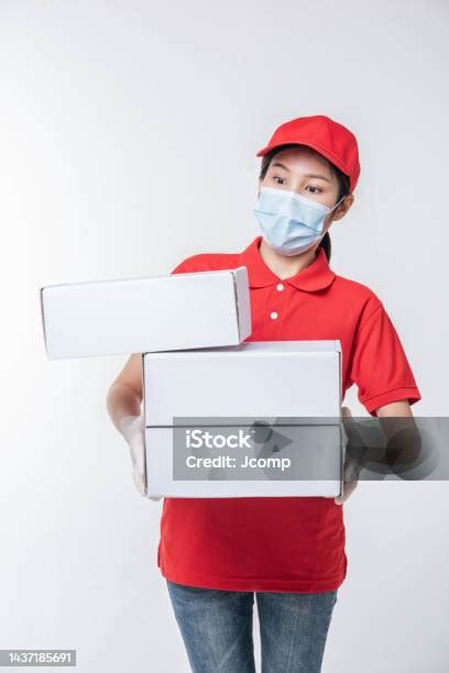 빨간 모자 빈 티셔츠 유니폼 얼굴 마스크 장갑을 낀 의식이 있는 젊은 배달원의 이미지는 밝은 회색 배경 스튜디오에 격리된 빈 흰색 판지 상자 팬데믹 코로나바이러스 바이러스