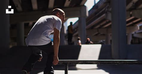 흰색 티셔츠와 검은 바지를 입은 남자가 검은 금속 막대에 앉아 있다 사진 Unsplash의 무료 마이애미 이미지