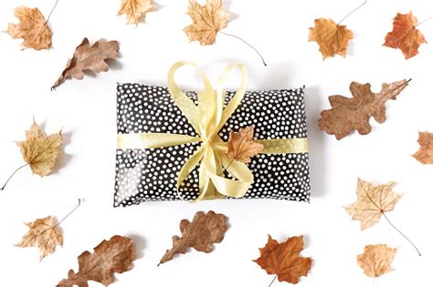 선물은 포장지로 감싸고 노란 리본으로 묶여 흰색 배경에 마른 단풍 나무 잎과 함께 놓습니다 생일 기념일 선물 기부에 축하의 가을