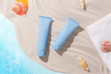 신선한 바다를 배경으로 모래 불가사리 조개껍데기 흰 수건 생동감 넘치는 파란색 화장품 튜브 2개가 있어 계절별 화장품 광고에 적합합니다 모형 배경 주제에 대한 스톡 사진 및