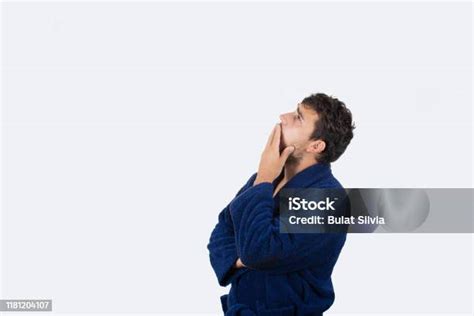 파란 목욕 가운을 입고 졸린 젊은 사업가가 위를 쳐다보고 하품하는 것은 흰색 배경에서 고립 된 잠을 자야하는 피곤함을 느낍니다 기진맥진에 대한 스톡 사진 및 기타 이미지