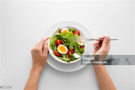 젊은 여자는 직접 위에서 본 흰 그릇에 신선한 샐러드 식사를 먹고 유기 야채와 포크를 들고 여성 손 간식 접시 위에서 본 최고의