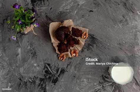 회색 콘크리트 배경에 비올라 삼색 꽃다발을 달고 있는 꽃병 옆에 초콜릿 컵케이크와 우유 한 잔이 표면에 서 있습니다 껍질을 벗긴 호두가 옆에 누워 있습니다 꽃 식물에 대한