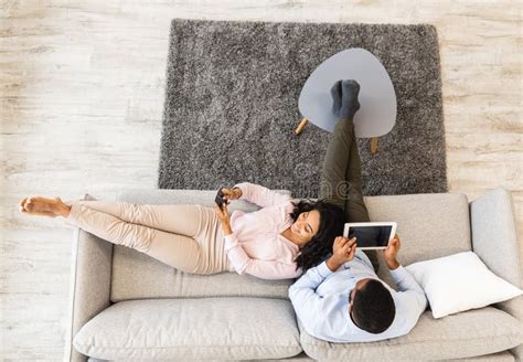African American Couple Sitting On Couch Using Tablet And Smartphone