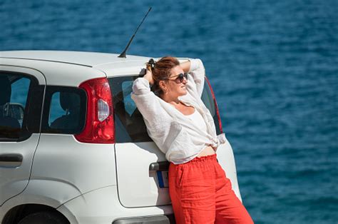 선글라스를 쓴 외로운 여자는 길가의 작은 흰색 차에 주차된 그리스 케팔로니아 섬의 이오니아 바다 풍경을 즐기고 있다 여름 방학 또는 자동차 여행 개념 카셰어링에 대한 스톡