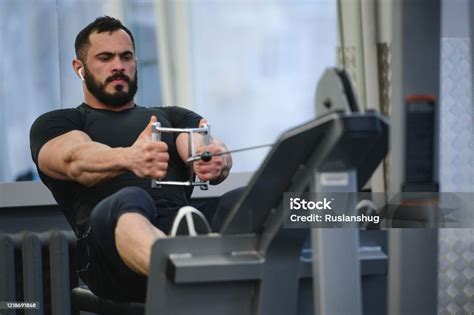 수염 앉아 와 젊은 활성 백인 남성의 스포츠 체육관에서 피트니스 훈련 과 운동 장비에 무거운 무게를 당기는 동기 부여 헤드폰을 착용 음악을 듣고 강사에 대한 스톡 사진 및