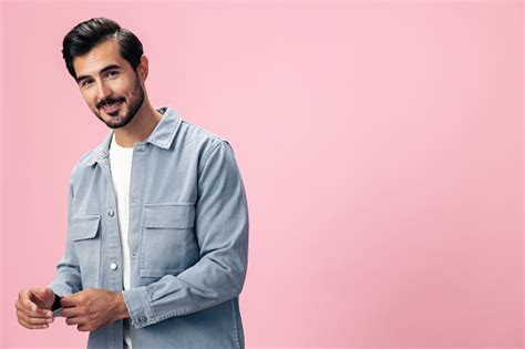 흰 티셔츠와 청바지에 분홍색 배경에 수염을 기르고 아름다운 미소를 지으며 그의 얼굴에 미소와 즐거운 감정을 가진 세련된 갈색 머리 남자의 초상화 복사 공간 25 29세에