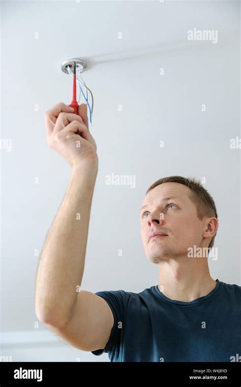 Installing A Spotlight In The Room The Man Is Fixing The Bracket For The Ceiling Lamp Stock
