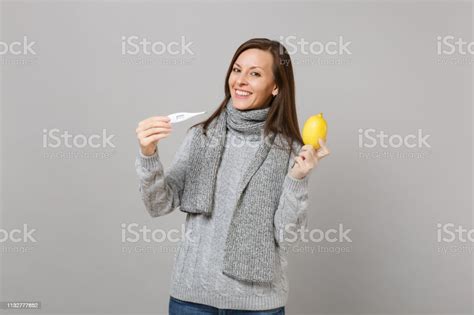 회색 스웨터에 웃는 젊은 여자 스튜디오에서 회색 벽 배경에 고립 된 레몬 온도계를 들고 스카프 건강 한 라이프 스타일 아픈 질병
