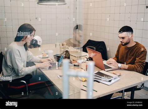 Young Male And Female Computer Programmers Using Laptops For Encryption At Desk In Small Office