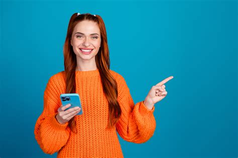 쾌활한 예쁜 아가씨 옷을 입은 오렌지 풀오버 Sms 작성 현대 가제트 가리키는 빈 공간 절연 블루 컬러 배경의 사진 20 24세에 대한 스톡 사진 및 기타 이미지 Istock