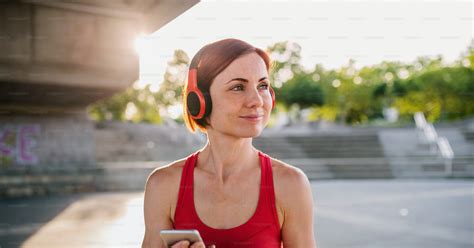 도시에서 헤드폰을 끼고 휴식을 취할 때 스마트폰을 사용하는 젊은 여성 주자 사진 Unsplash의 슬로바키아 이미지