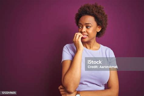 고립 된 보라색 배경 위에 아프리카 머리를 가진 젊은 아름다운 아프리카 계 미국인 여성은 손톱을 물고 손톱을 물어 뜯는 손에 손을 대고 스트레스를 받고 긴장합니다 불안 문제