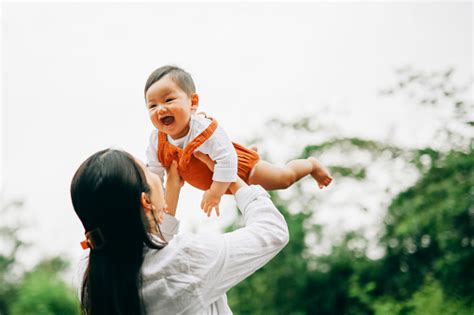 야외에서 즐거운 아시아 여성과 그녀의 어린 아기 사이의 부드러운 순간 여성의 미소는 따뜻함과 사랑을 발산하며 기쁨과 만족의 진심 어린 분위기를 조성합니다 흐릿한 녹색 배경이