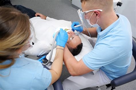 클리닉에서 치아 청소 및 연마 받기 의자에서 환자를 치료하는 치과 의사 파란 장갑을 낀 의사는 환자의 치아에 연고를 바르고 청소해야 할 플라크가있는 곳을 보여줍니다 거울에