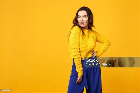 스웨터에 열정적 인 젊은 여자의 초상화 파란색 바지는 노란색 오렌지 벽 배경에 고립 된 허리에 팔 Akimbo 서 서 사람들은 진심으로 감정 라이프 스타일 개념입니다 복사