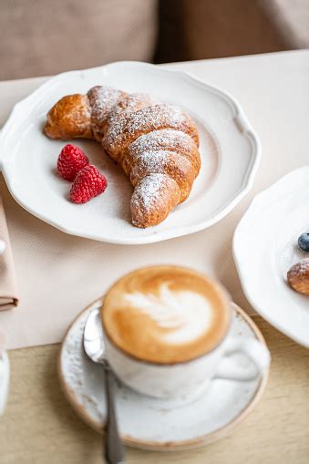 레스토랑에서 흰색 접시에 크루아상을 곁들인 커피 카푸치노 가벼운 아침 식사 신선한 따뜻한 페이스트리와 라즈베리 0명에 대한 스톡