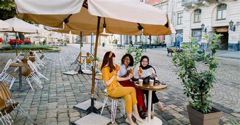 도시 생활 방식 점심 시간 우정 개념 세 명의 매력적인 미소를 짓는 젊은 다양한 여성 친구들이 이야기하고 웃고 야외 카페의 테이블에 앉아 크루아상과 함께 커피를