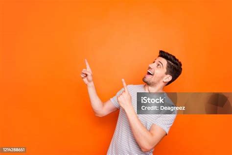사진 의 매력적인 재미 미친 사람 보유 손 손가락 직접 빈 공간 흥분 좋은 분위기 판매 담당자 착용 스트라이프 티셔츠 고립 밝은 오렌지 색 배경 가리키기에 대한 스톡 사진