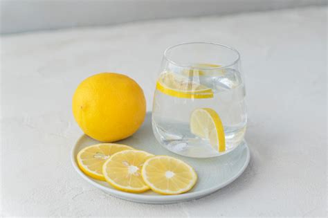 레몬 슬라이스가 있는 투명한 물 한 잔의 각도보기 레몬 조각 3개가 근처의 흰색 접시에 놓여 있습니다 감귤류 과일에 대한 스톡 사진 및 기타 이미지 Istock