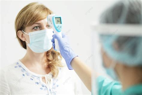 A Female Medical Professional In Uniform Uses A Temperature Measuring Device To Check A Womans