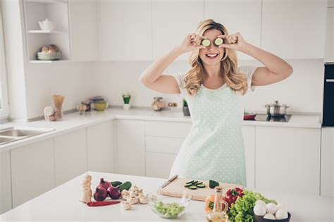 가벼운 부엌에 서있는 오이와 함께 그녀의 얼굴을 닫고 물결 모양의 곱슬 머리 커버를 가진 재미 아름다운 여성 요리사의 Porrait 가정 생활에 대한 스톡 사진 및 기타