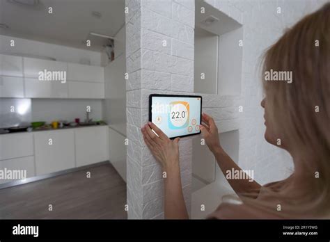 Woman Controlling Home With A Digital Touch Screen Panel Installed On The Wall In The Living