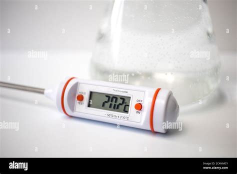 A Digital Thermometer In Front Of A Liquid In A Glass Erlenmeyer Flask On A White Background