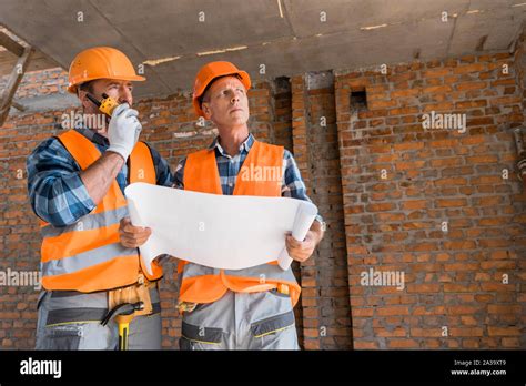Constructor Holding Blueprint Near Handsome Coworker With Walkie Talkie
