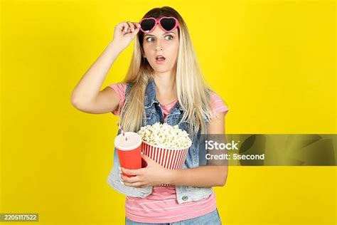 노란색 배경에 팝콘과 종이컵이 든 양동이를 들고 선글라스를 낀 젊은 여자 20 24세에 대한 스톡 사진 및 기타 이미지 20 24세 건강한 생활방식 건강한 식생활