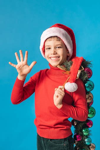 산타 모자를 쓴 쾌활한 아이는 파란색 배경 크리스마스 및 휴일 개념 모형에 크리스마스 장식 공을 들고 있습니다 알파 세대와 알파 세대 자녀 12월에 대한 스톡 사진 및 기타