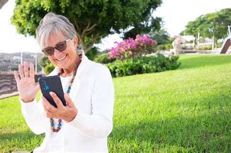 스마트 폰과 화상 통화에서 아름다운 노인 여성 목걸이와 선글라스를 입고 흰색 미소 성숙한 회색 머리 여자 그린 가든 공공 공원의 배경 70 79세에 대한 스톡 사진 및 기타