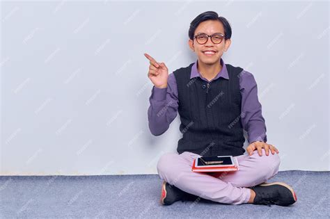 흰색 배경 디지털 기술 개념에 격리된 다리를 꼬고 바닥에 앉아 있는 동안 안경을 끼고 복사 공간을 가리키는 웃고 있는 전문 젊은