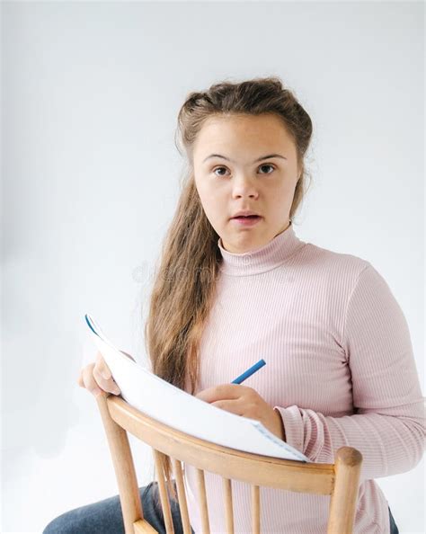 A Focused Young Woman With Down Syndrome Sits In A Wooden Chair
