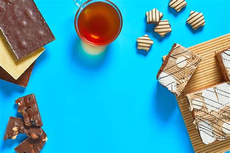 차 초콜릿 바 사탕의 전체 유리 컵 근처 대나무 매트에 슬라이스 체크 무늬 직사각형 케이크는 파티의 파란색 테이블에 놓여있다 축