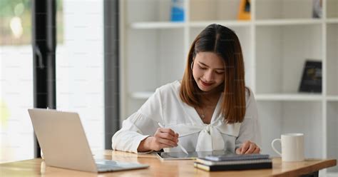 스타일러스 펜을 들고 사무실 유리 벽을 배경으로 한 현대적인 작업 테이블에서 노트북 앞에 앉아 컴퓨터 태블릿에 그림을 그리는 데 사용하는 여성 사진 Unsplash의