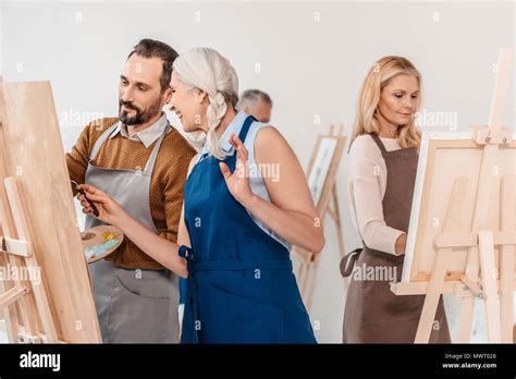 Adult Students In Aprons Painting On Easels During Art Class Stock