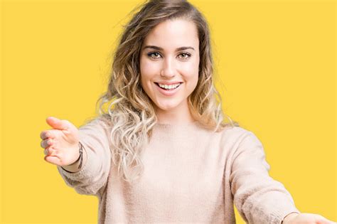 아름 다운 젊은 금발 여자 카메라 포옹에 대 한 두 팔을 벌려 웃 고 보고 격리 된 배경 위에 Sweatershirt를 입고 명랑 식 수용 행복입니다 곱슬 머리에 대한 스톡