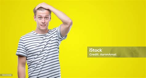 줄무늬 선원 머리에 손으로 강조 했다 T셔츠를 입고 젊은 잘생긴 금발 남자 충격 수치심과 깜짝 얼굴로 분노와 좌절 두려워 하 고 실수에 대 한 화가 T 셔츠에 대한 스톡