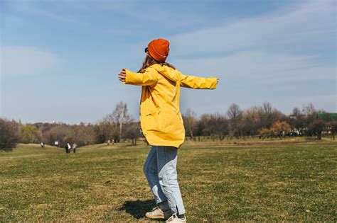 노란 재킷을 입고 뒤에서 빨간 모자를 쓴 소녀가 공원의 잔디밭에서 즐겁게 회전합니다 30 34세에 대한 스톡 사진 및 기타 이미지 30 34세 가을 개 산책 Istock