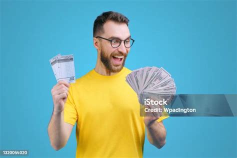 복권 티켓과 도박 돈 승리 개념으로 손에 달러 Bancknotes의 와드와 함께 포즈 노란색 티셔츠에 행복한 기쁘게 수염 남자의