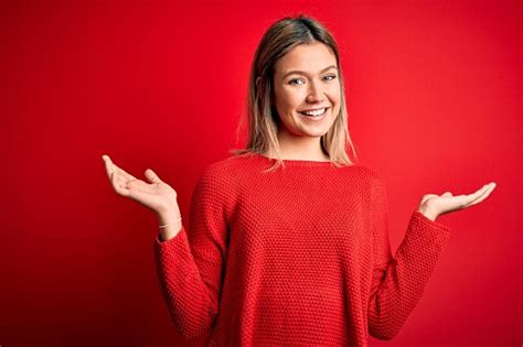 젊은 아름다운 금발 의 여자 입고 캐주얼 스웨터 위에 빨간 고립 된 배경 미소 보여주는 양손 오픈 손바닥 제시 및 광고 비교 및 균형 손바닥에 대한 스톡 사진 및 기타