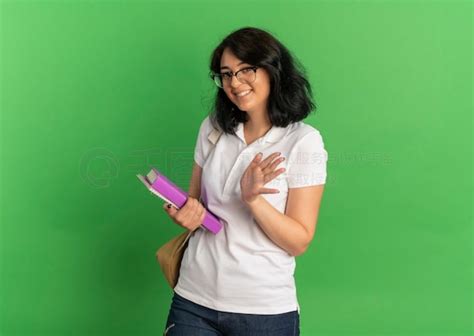 女学生高清图片 戴着眼镜、背着背包的年轻微笑漂亮白人女学生看着相机，举起手拿着绿色的书本，上面有复印空间 产品实拍免费下载 格式 编号51027234 千图网