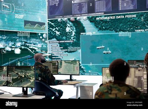 Army Personnel Monitoring Surveillance Imagery From Satellite System On Big Screen In Control