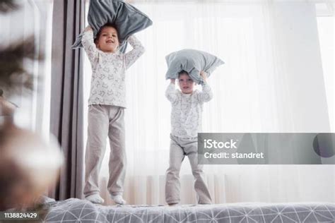 เด็กเล่นบนเตียงพ่อแม่ เด็กตื่นขึ้นมาในห้องนอนสีขาวแดด เด็กชายและเด็กหญิงเล่นในชุดนอนที ภาพสต็อก