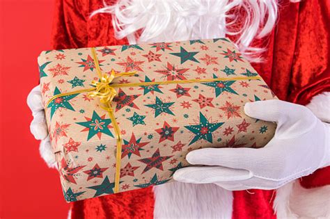 빨간색 배경에 선물을 들고 있는 장갑을 낀 산타클로스 옷을 입은 남자의 손의 세부 사항 크리스마스 축하 선물 소비주의 및 행복